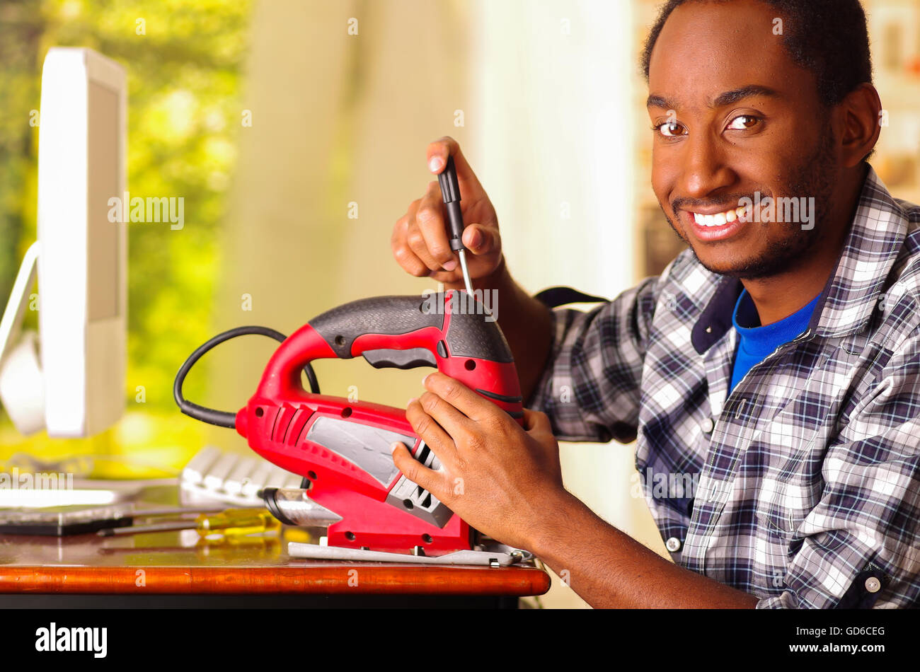 Man sitting by desk repairing handheld jigsaw using screwdriver ...