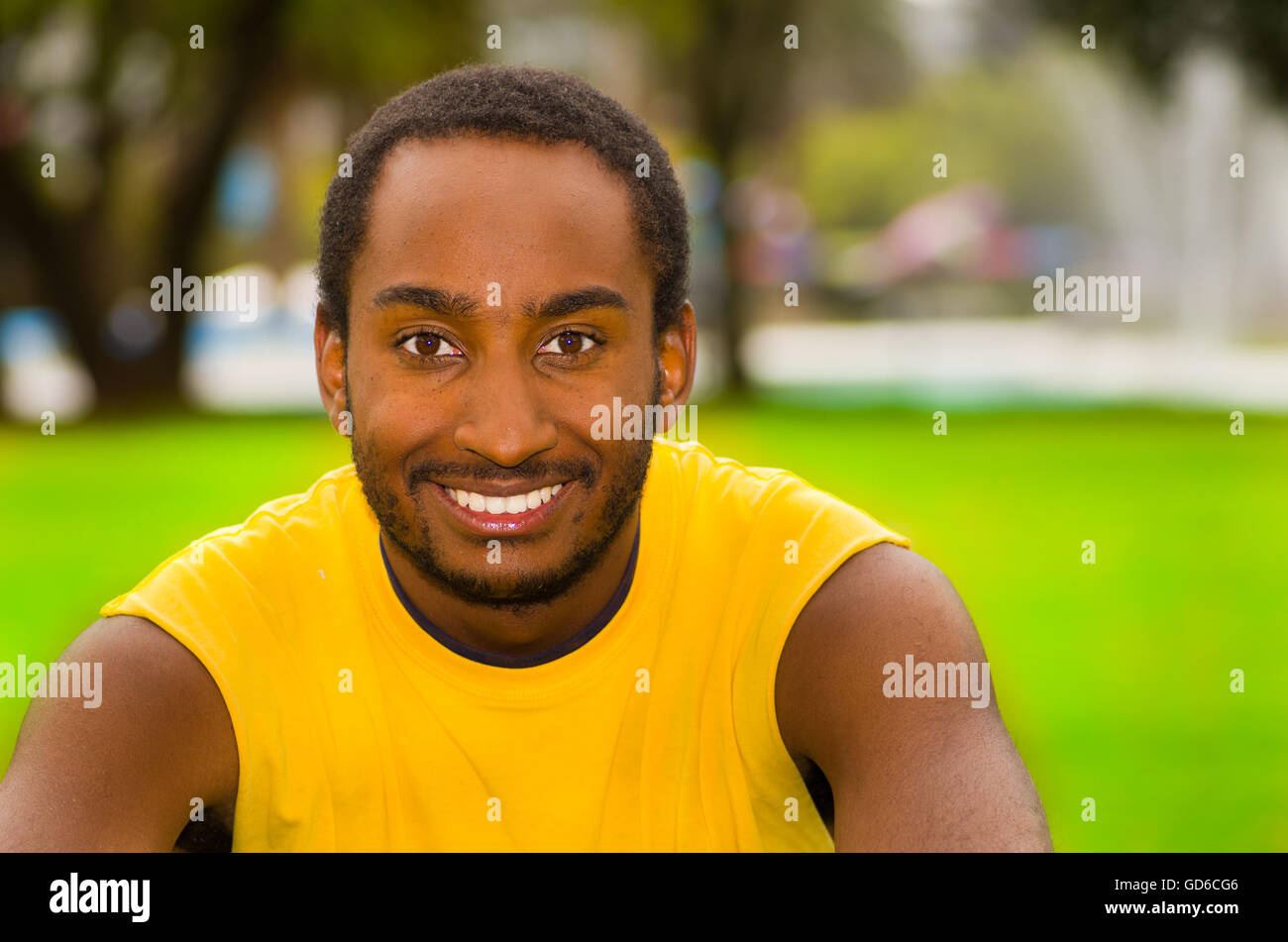 Man wearing yellow shirt sitting in park sorrounded by green grass and ...