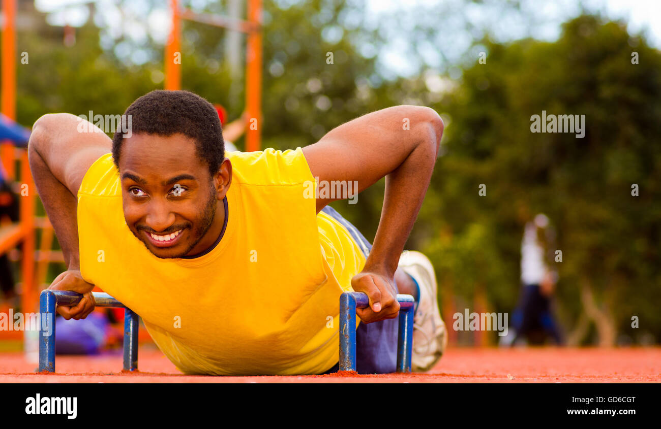 Man wearing yellow shirt doing push-ups at outdoors training facility ...