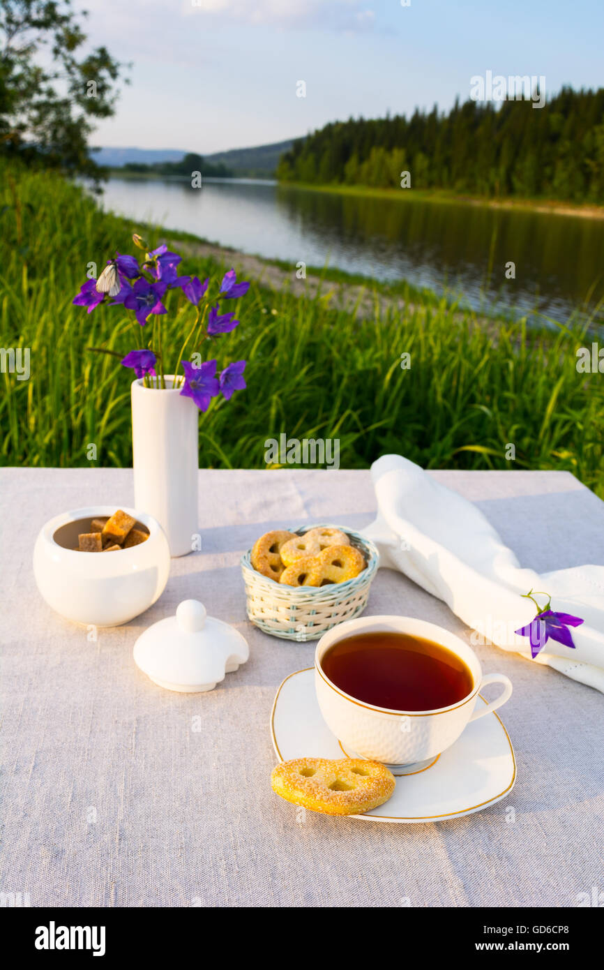 Evening tea sunset river view. Cup of tea and cookies in small wicker ...