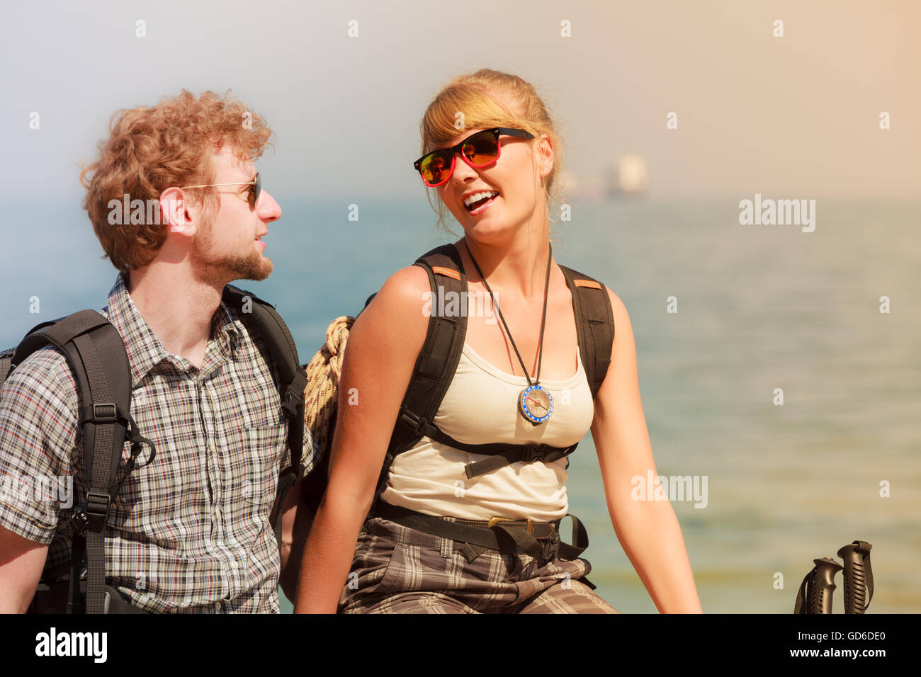 Two happy young people tourists hiking by sea ocean water. Backpackers ...
