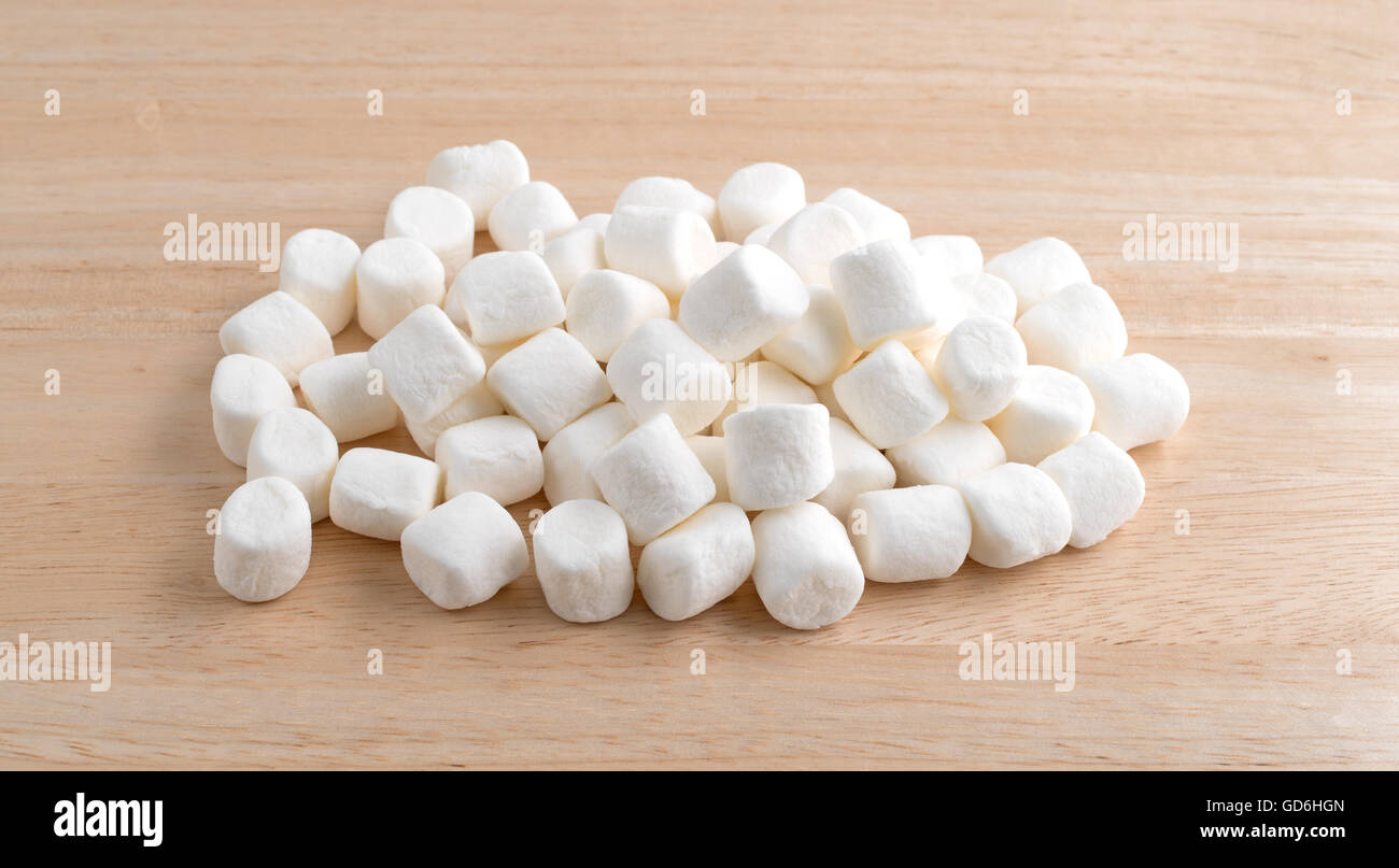 Small bite size marshmallows on a wood cutting board illuminated with ...