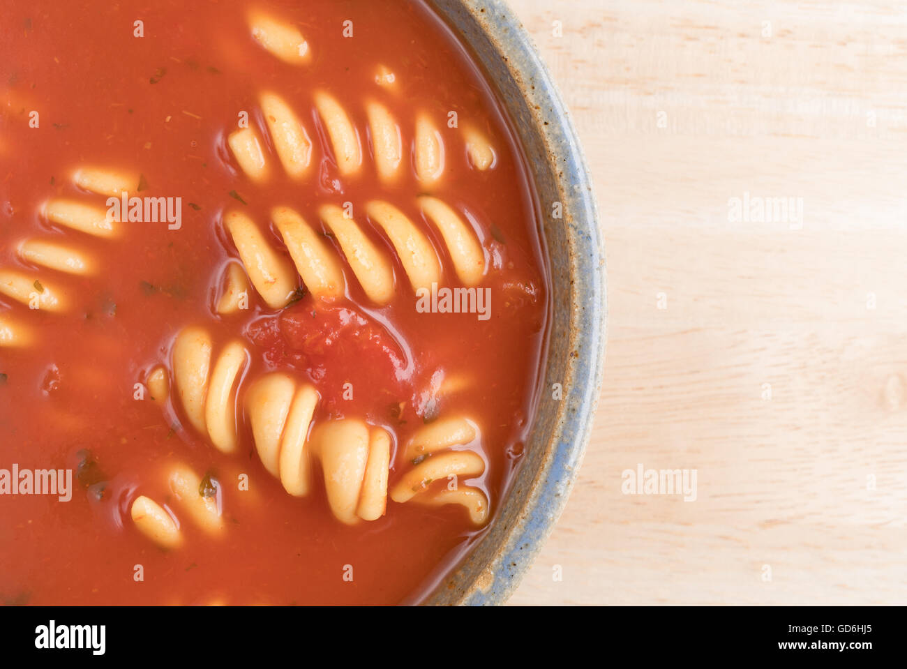 Rotini tomato soup in an old stoneware bowl on a wood table top close ...