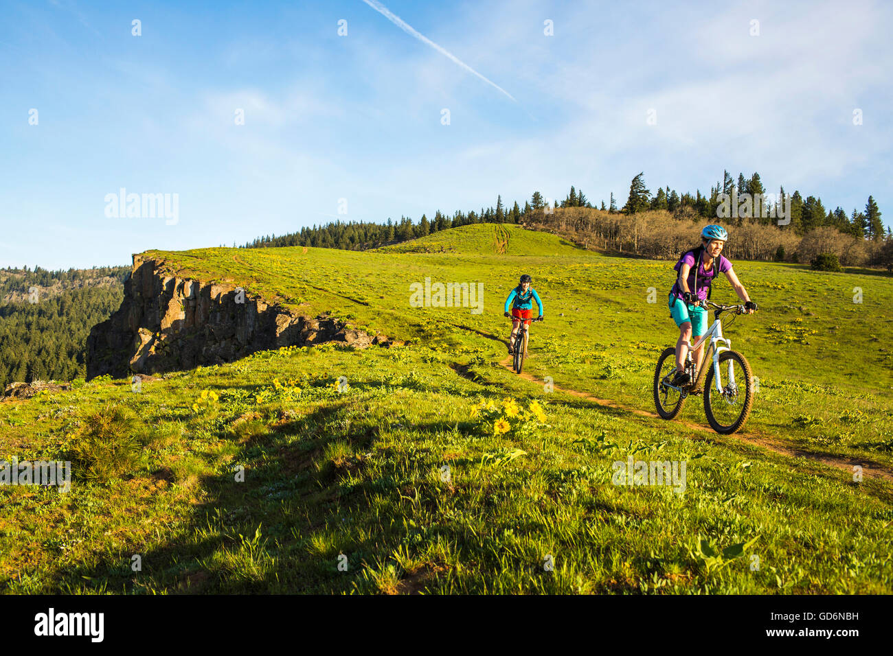 Two young women ride mountain bikes down a single-track trail through ...