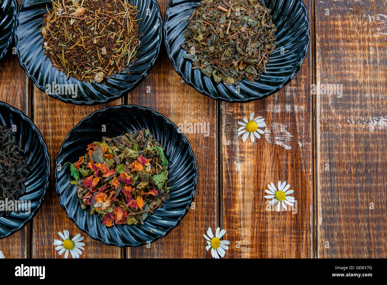 Different kinds of tea on plates on wooden background with flowers of ...