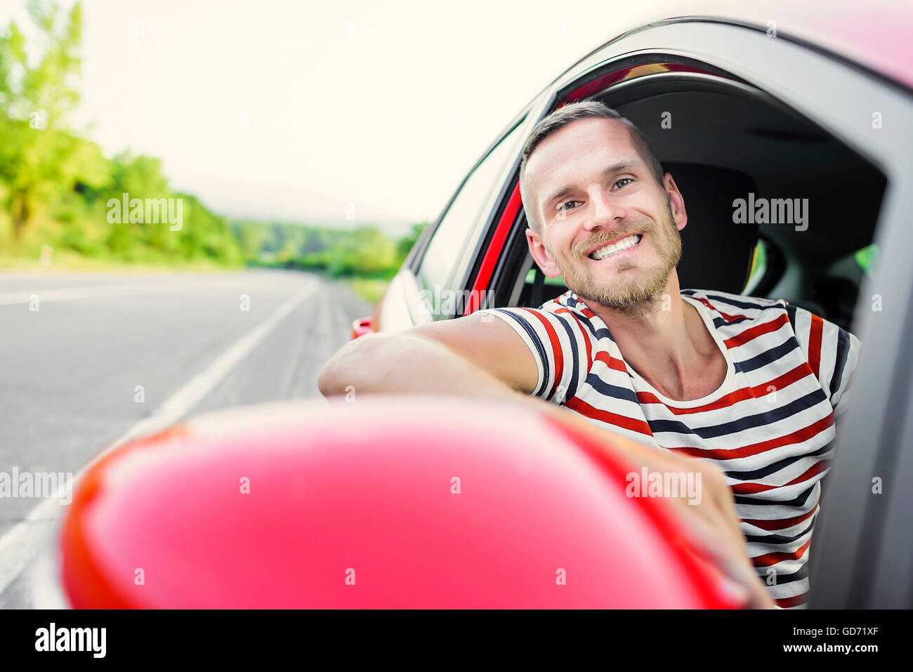 Driver. Smiling man in red car on the road at sunset Stock Photo - Alamy