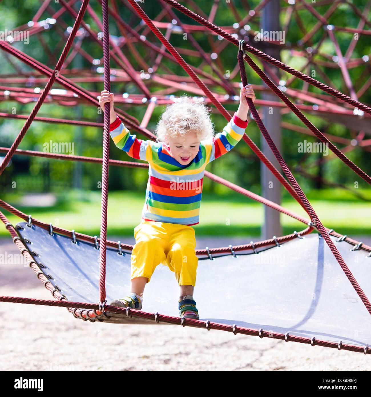 Active little child playing on climbing net and jumping on trampoline ...