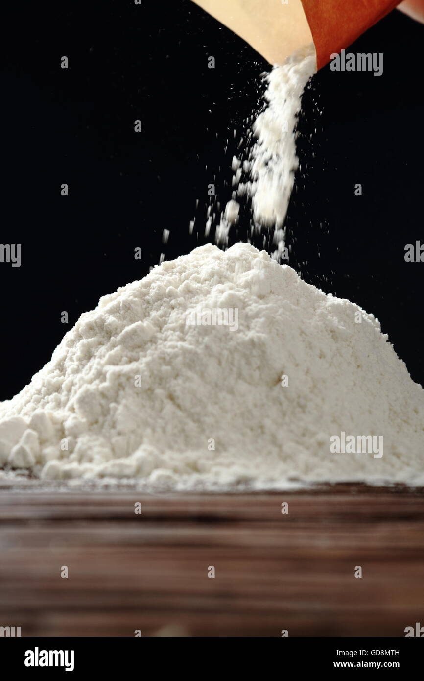 Pouring flour at black background Stock Photo - Alamy
