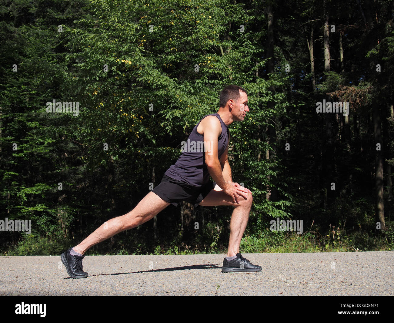 Caucasian male runner athlete stretching outdoors in forest. Forward ...