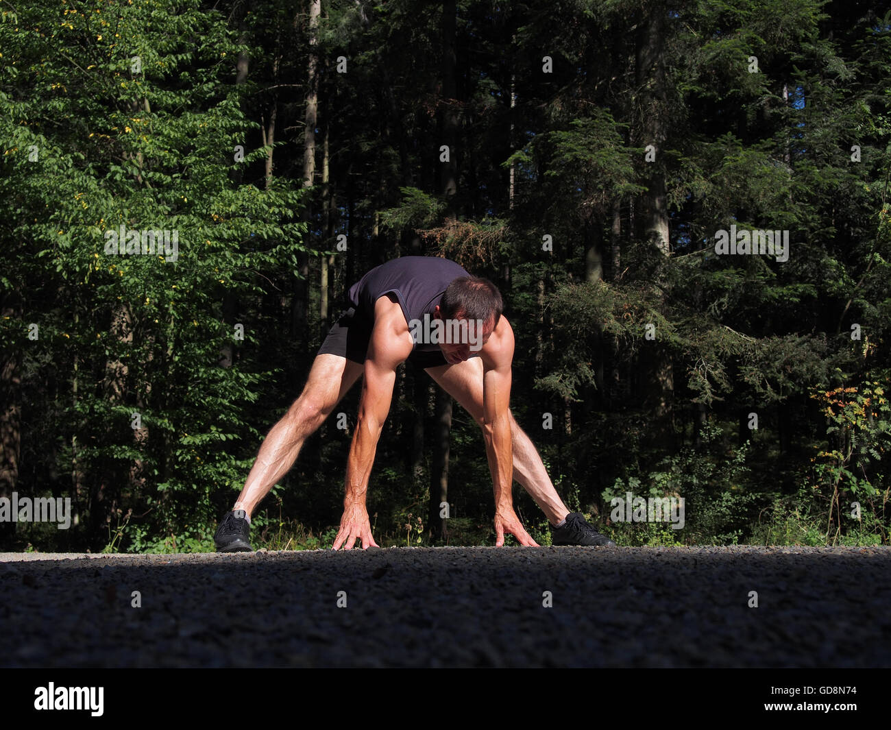 Caucasian male runner athlete stretching outdoors in forest. Wide ...
