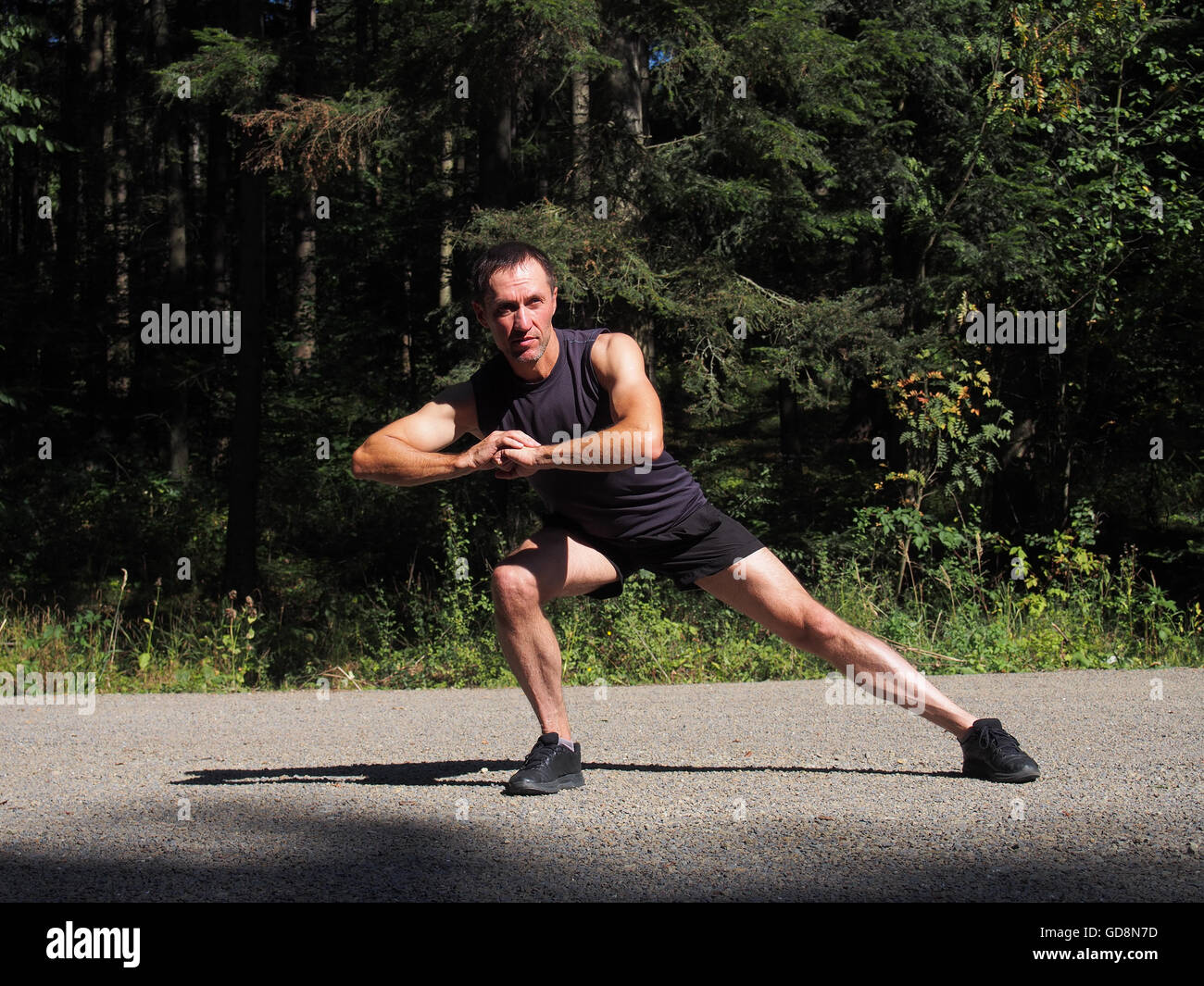 Caucasian male runner athlete stretching outdoors in forest. Side Lunge ...