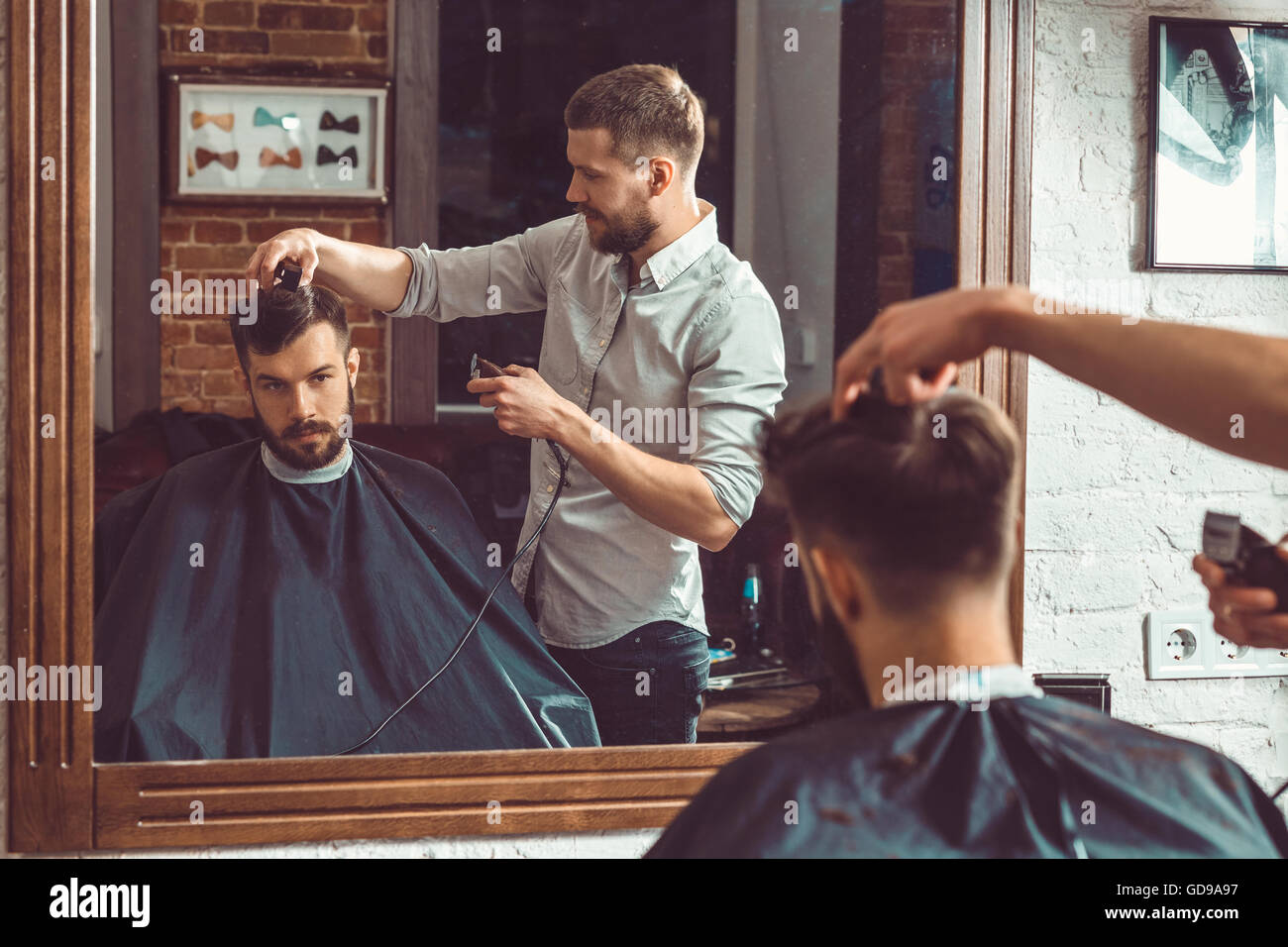 Young handsome barber making haircut of attractive man in barbershop ...
