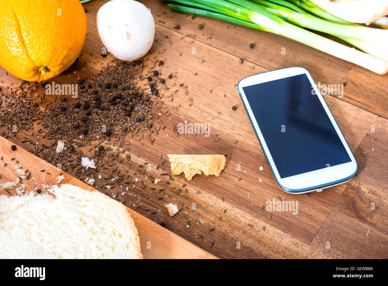 A smartphone lying in a natural kitchen with white bread, spices ...