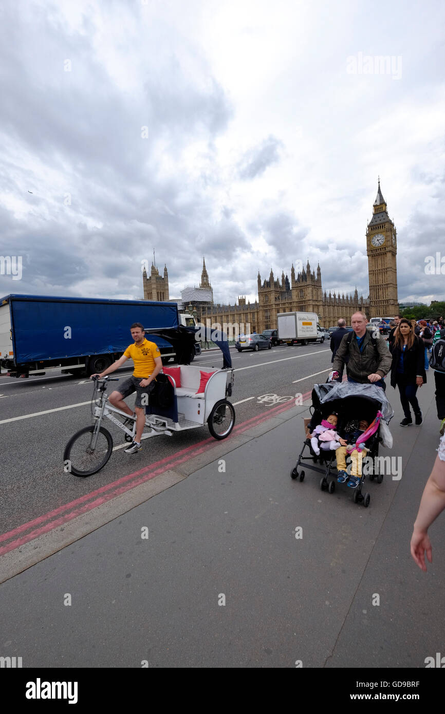 Pedestrians and a cycle cab cross Westminster Bridge Big Ben and Houses ...