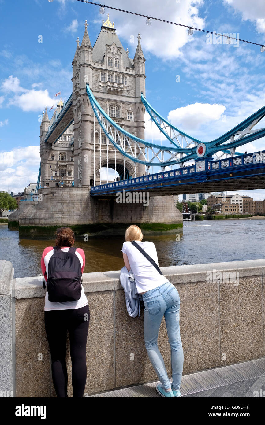 Tourists lean on the embankment wall looking at Tower Bridge a landmark ...