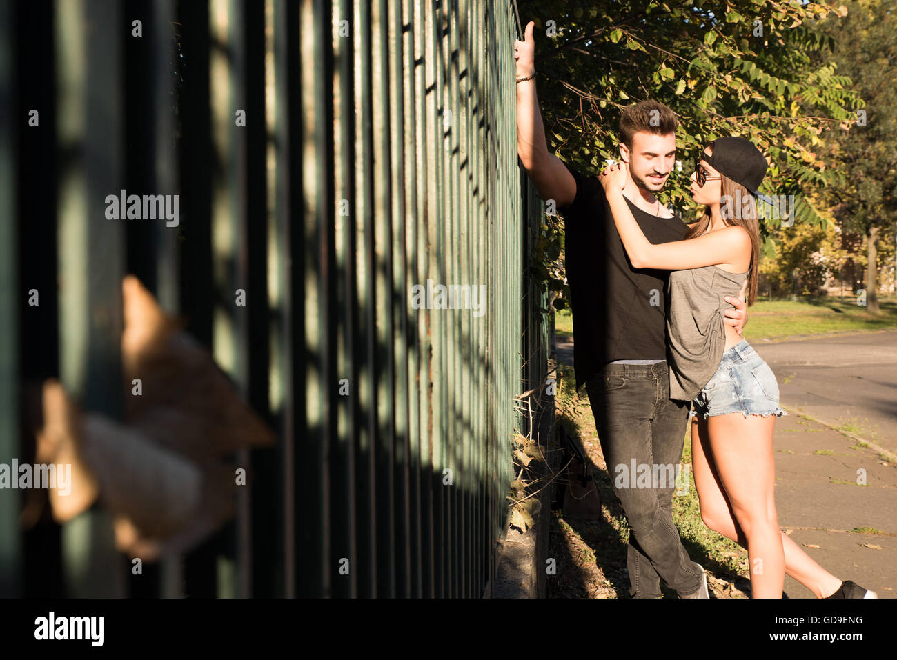 A young HipHop styled couple standing next to a fence during sunset in ...