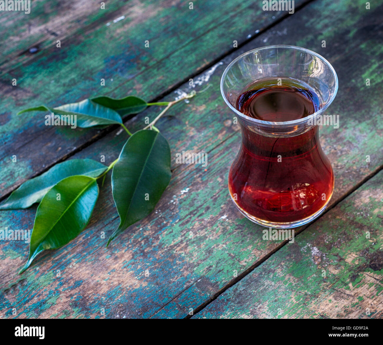 Black tea Turkish glass beaker with a green branch on the old table ...