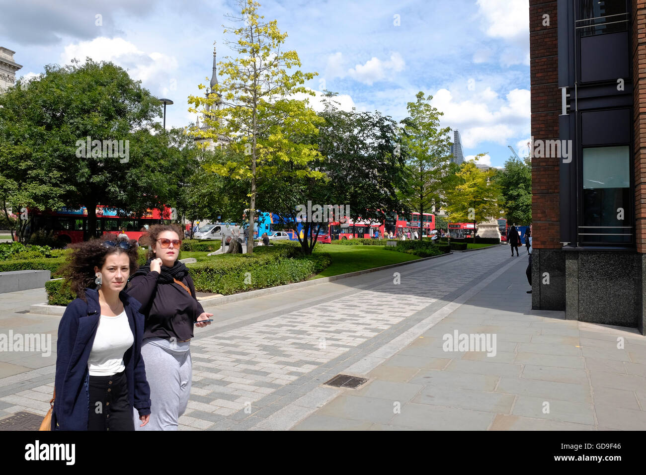 Pedestrians walk through a square in London with the London skyline in ...