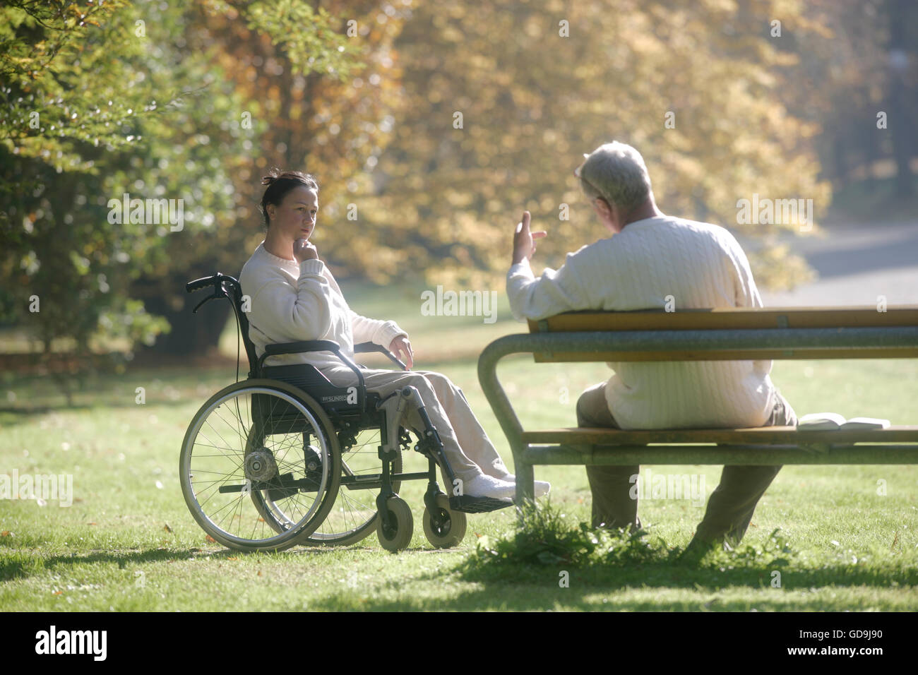 Woman sitting in a wheelchair, man sitting on a park bench Stock Photo ...