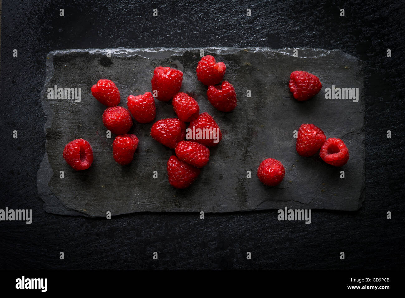 Wet raspberries on black slate board. Top view Stock Photo - Alamy