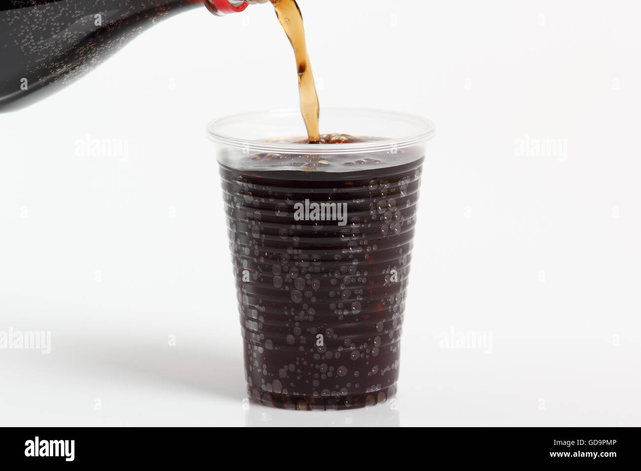 Pouring cola from bottle into plastic cup. Isolated on white background ...