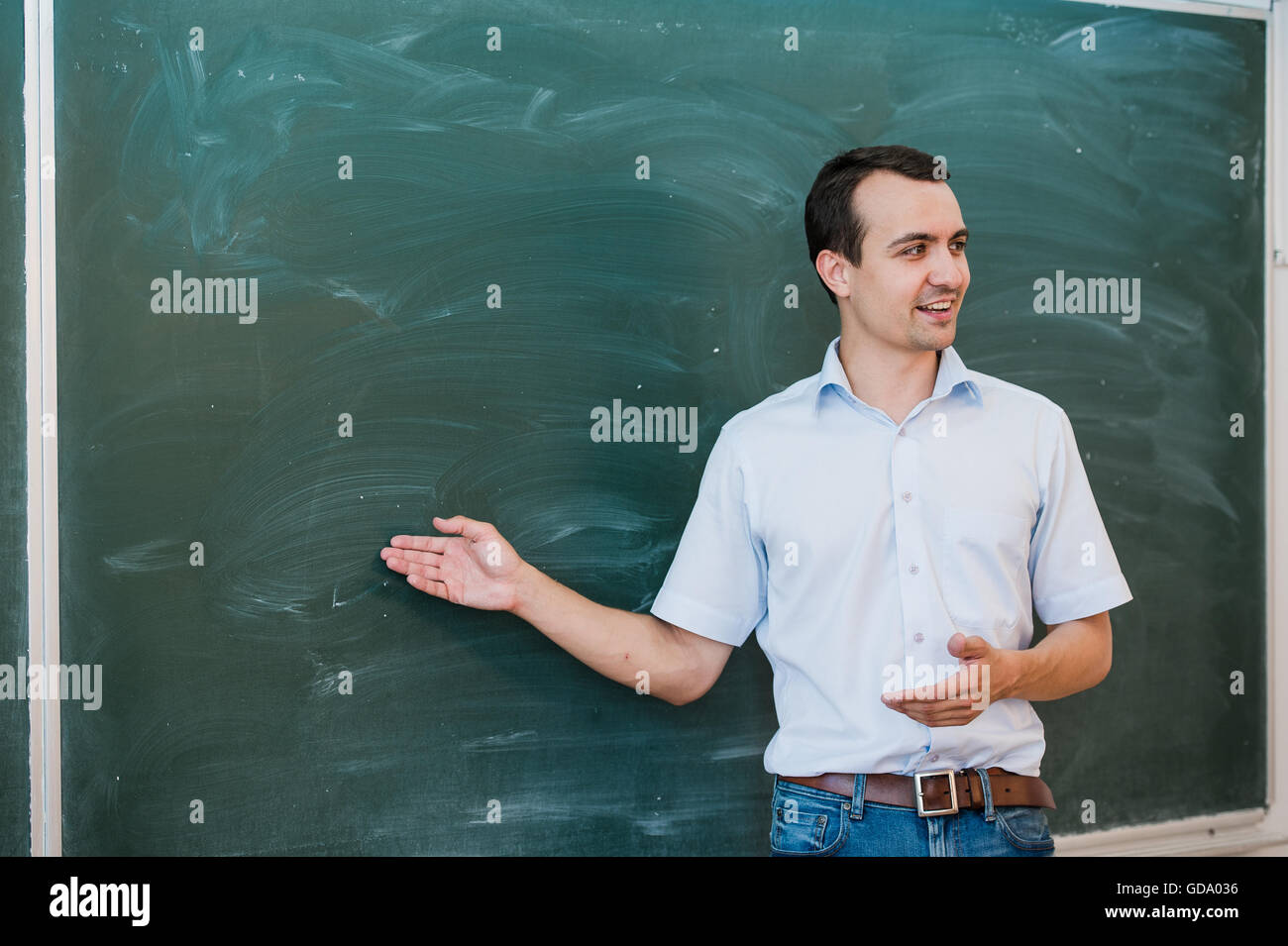 Young male teacher pointing at blank blackboard and talking Stock Photo ...
