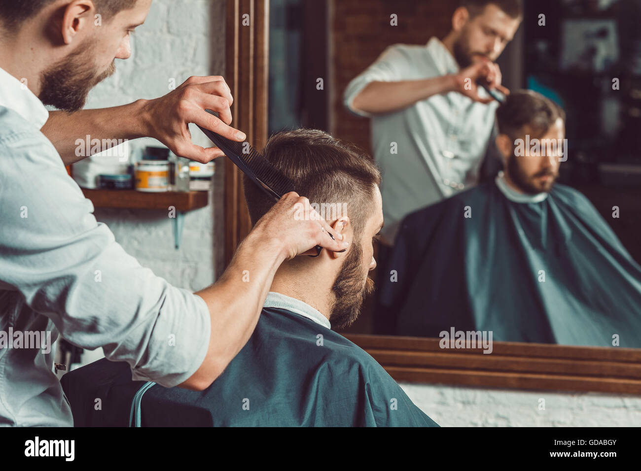 Young handsome barber making haircut of attractive man in barbershop ...