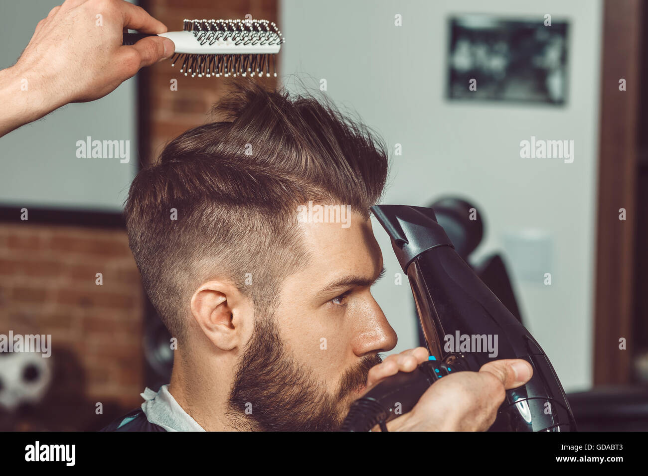 The hands of young barber making haircut to attractive man in ...