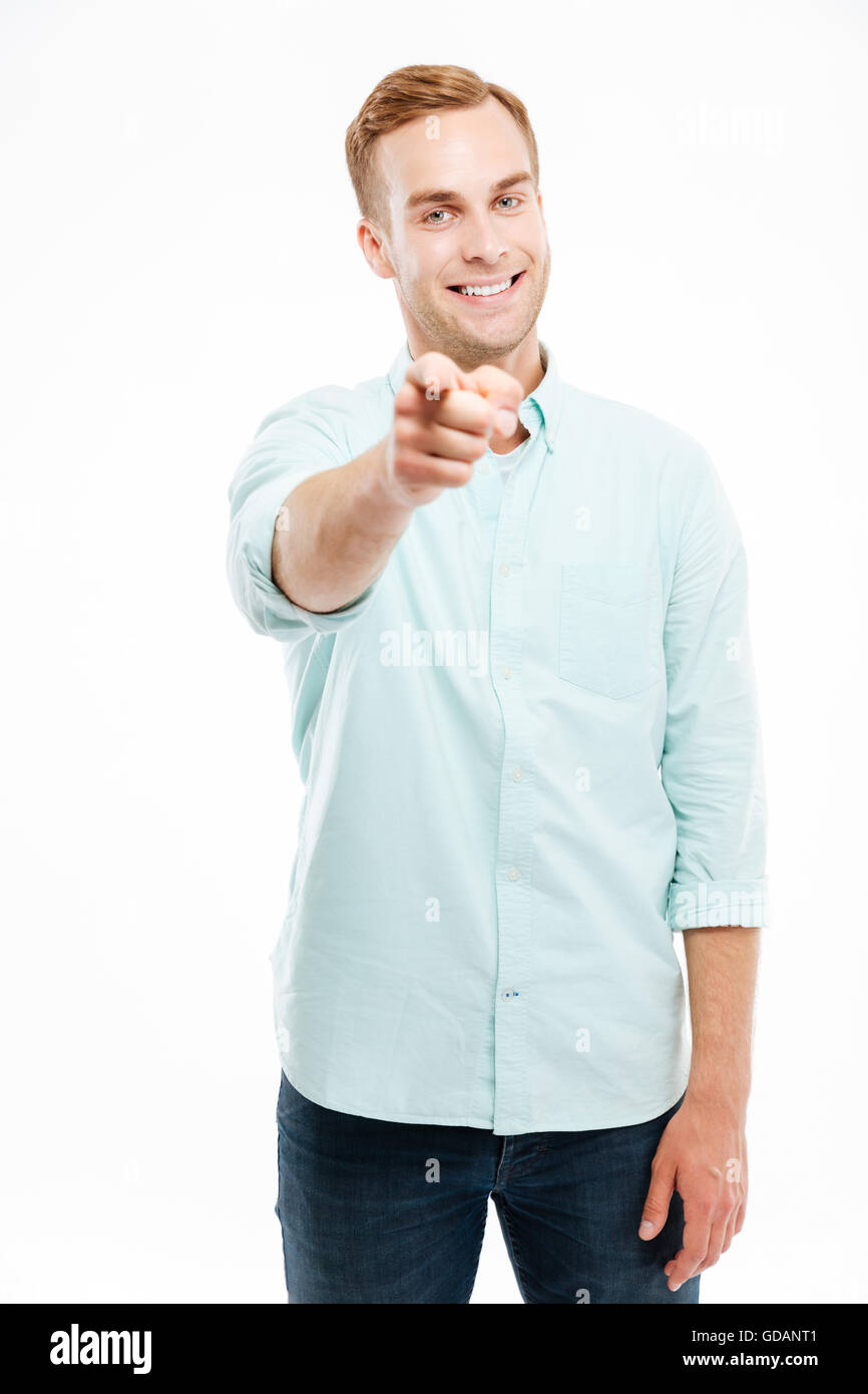 Cheerful attractive young man smiling and pointing at camera over white ...