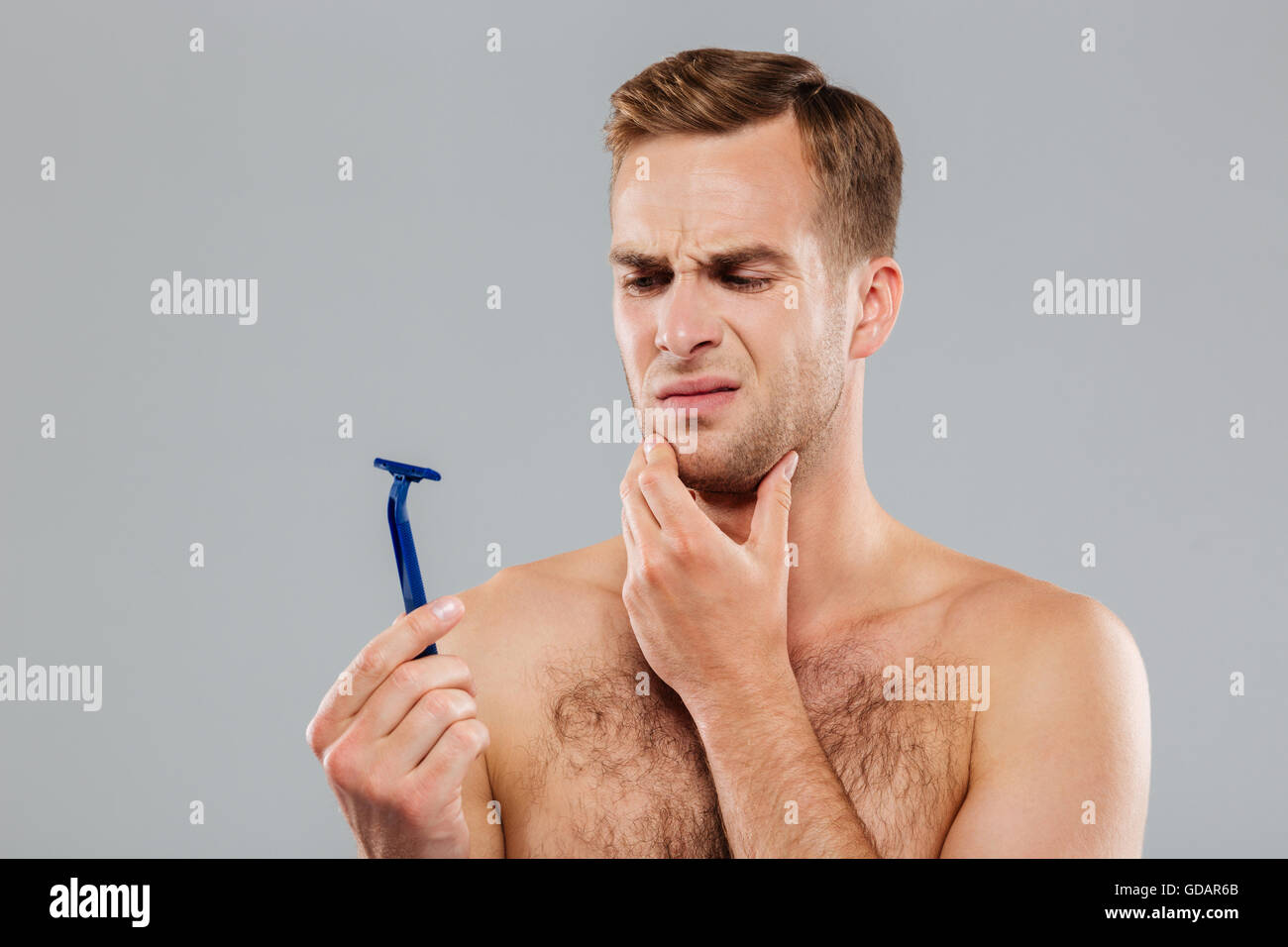 Young man holding razor and looking on it over gray background Stock ...