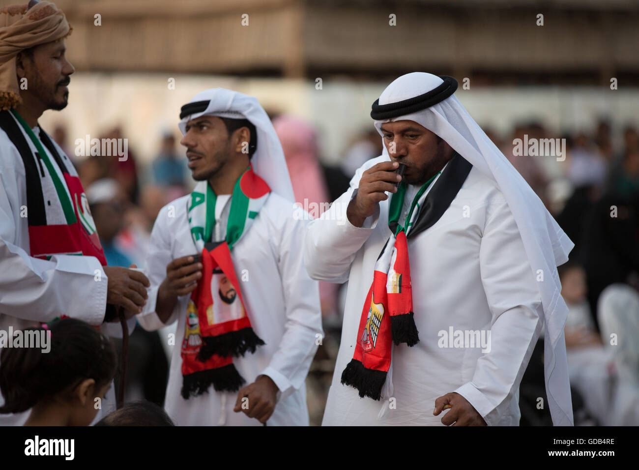 A group of Emirati men drink coffee with a crowd in the background at ...