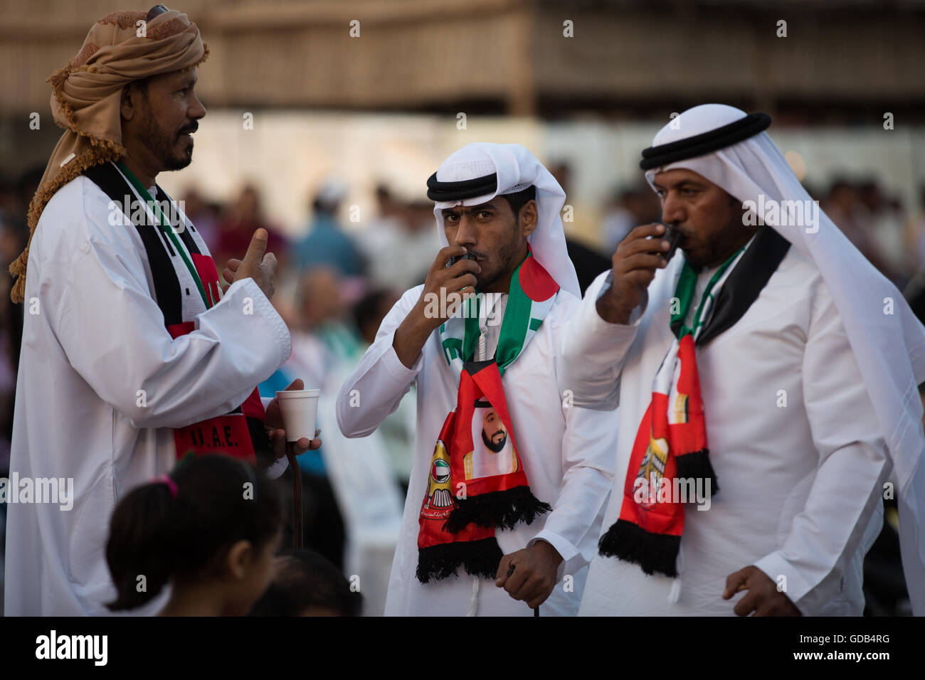 A group of Emirati men drink coffee with a crowd in the background at ...