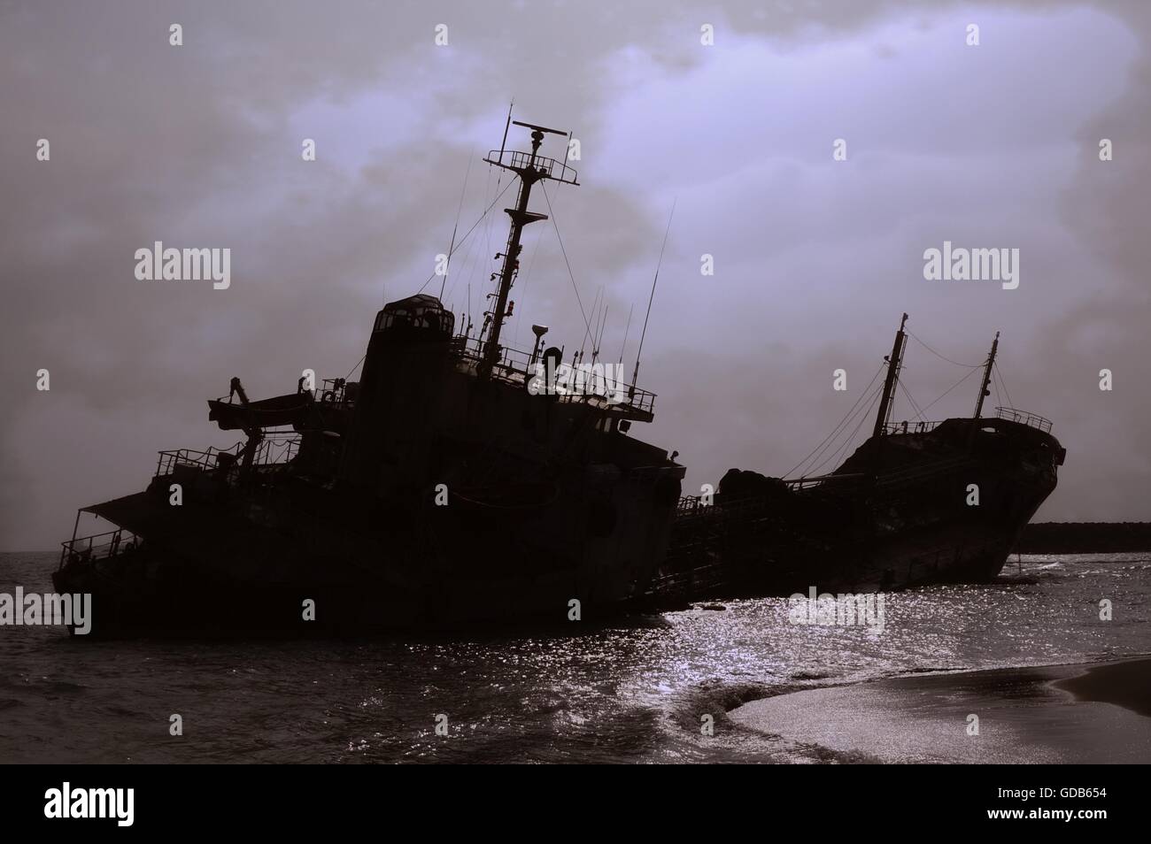 A beached ship lies in shallow waters with a gloomy sky in the ...