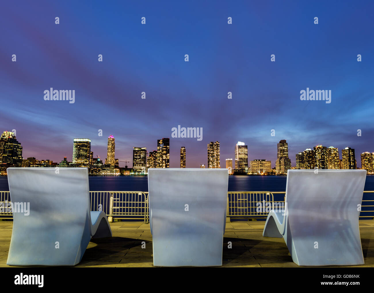 Three empty seats looking out over the river to a city skyline at night ...