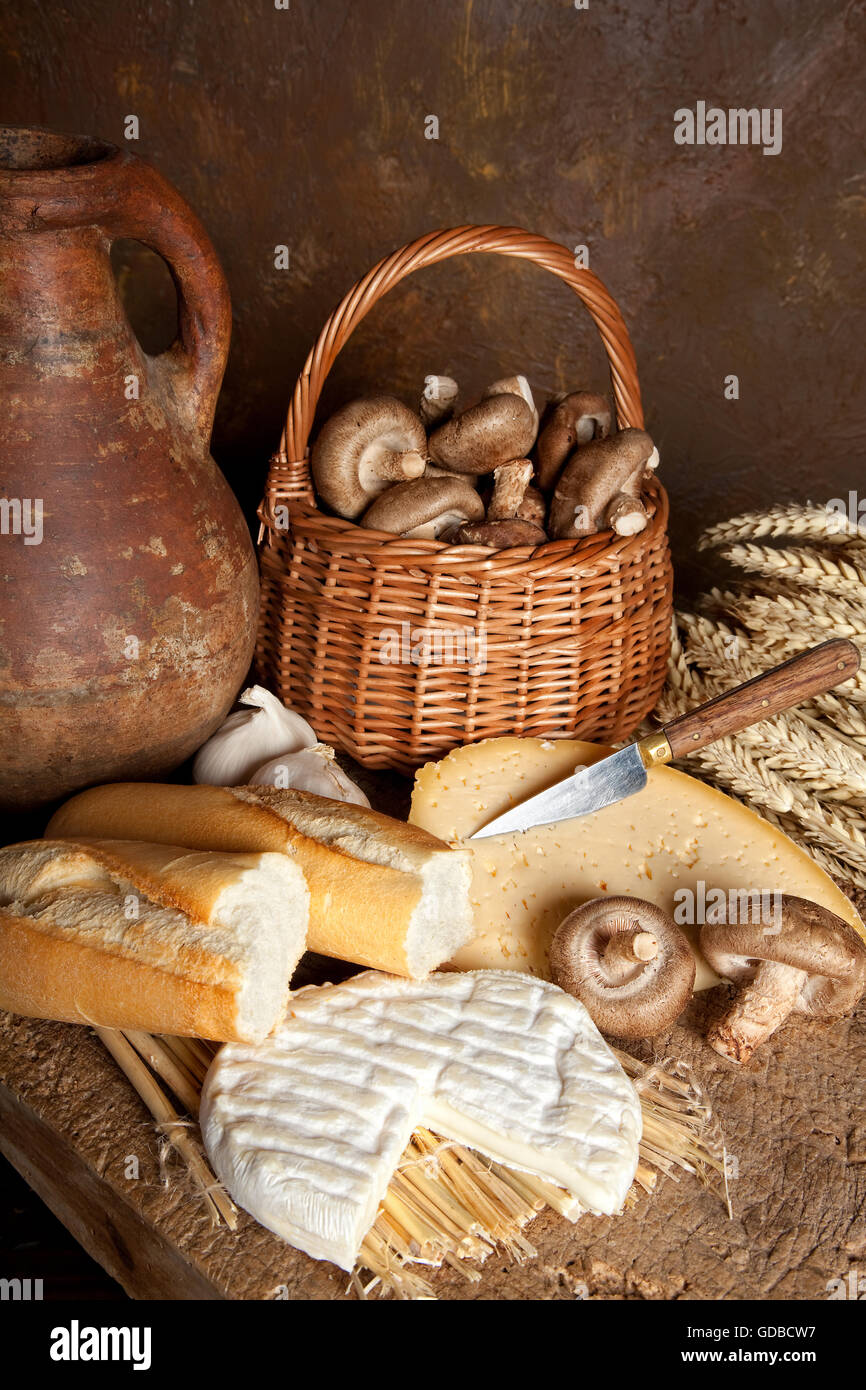 Country still life of rustic bread, cheese and an antique wine jug ...