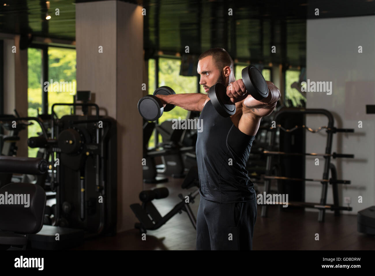 Big Man Standing Strong In The Gym And Exercising Shoulders With ...