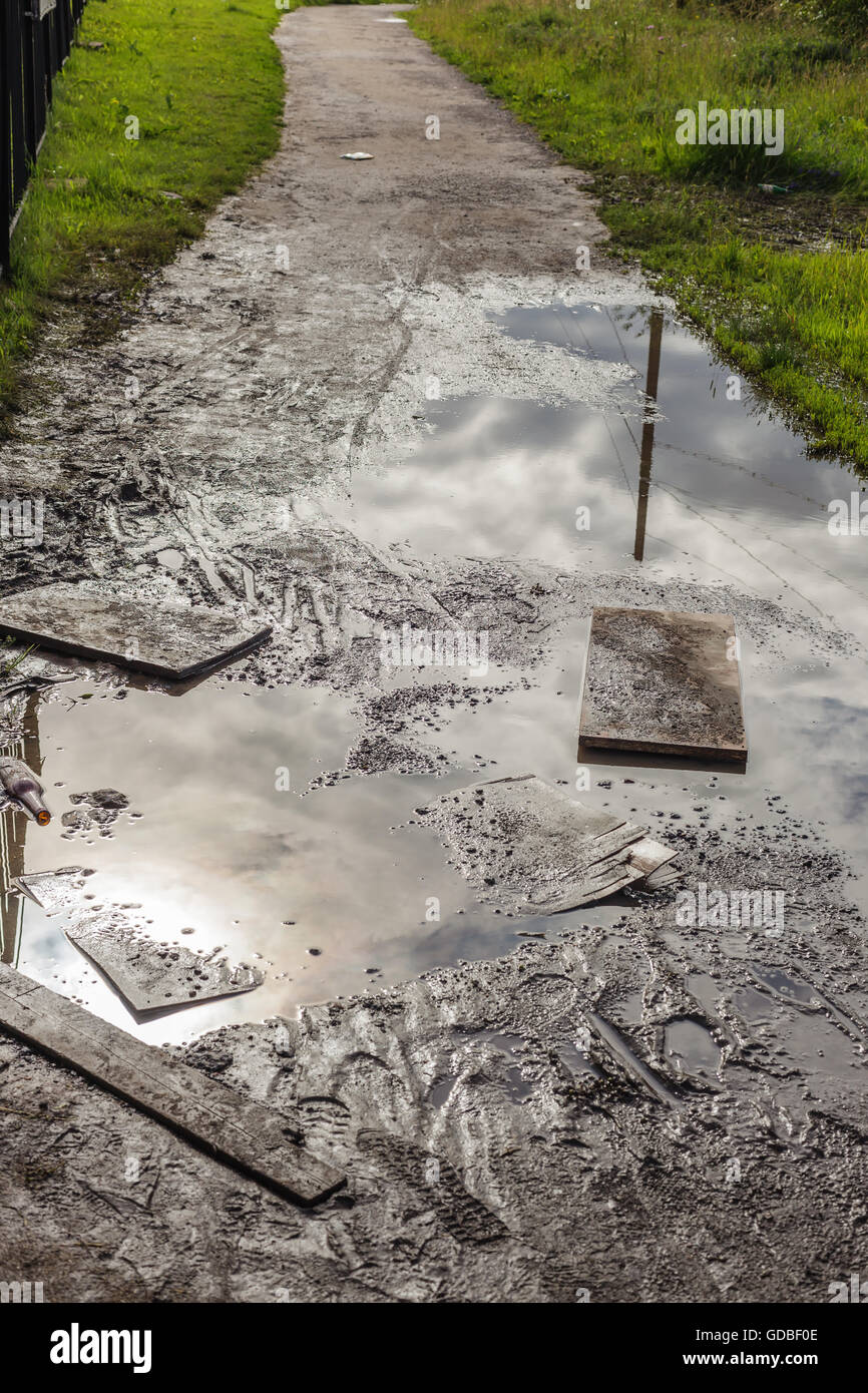 Dirty puddle on a country road with the reflection of sky and clouds ...