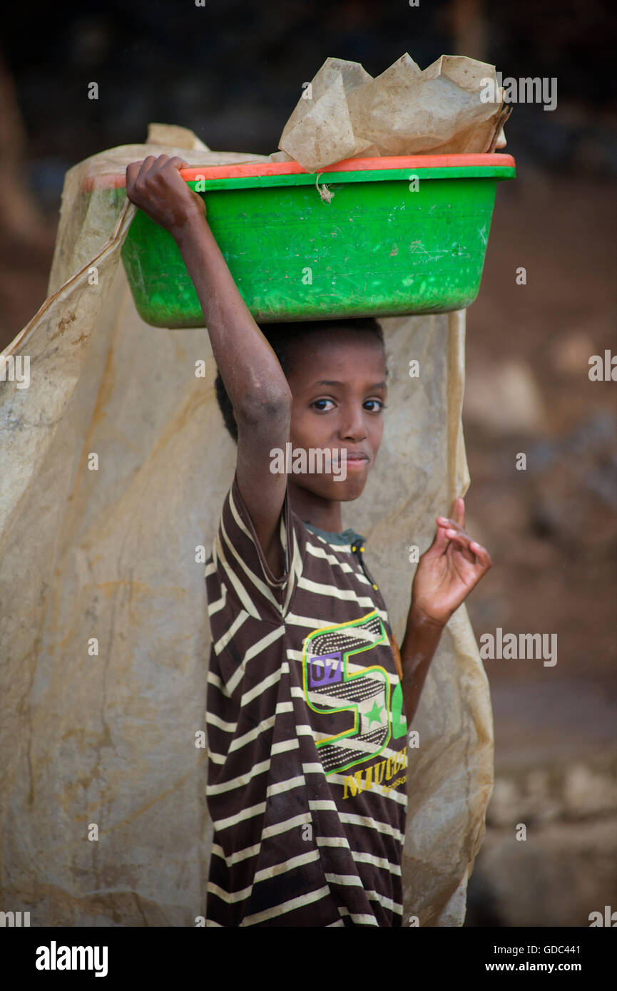 Ethiopian boy carrying bowls on his head and using plastic to shield ...
