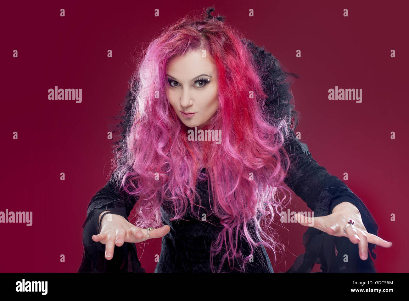 Scary witch with red hair performs magic on a pink background ...