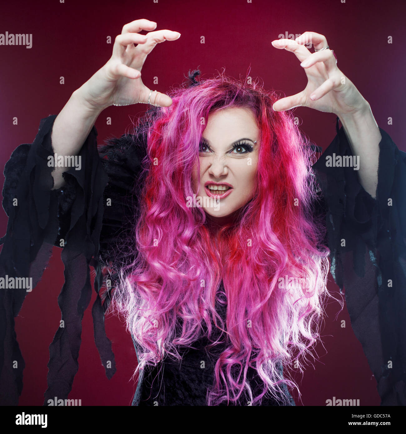 Scary witch with red hair performs magic on a pink background ...