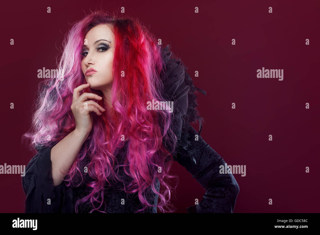 Scary witch with red hair performs magic on a pink background ...