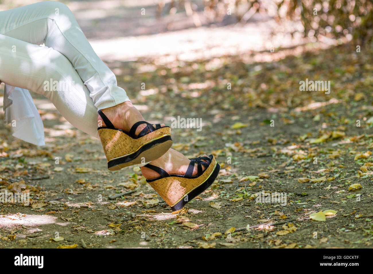 legs of woman sitting on bench in white trousers and high platform ...