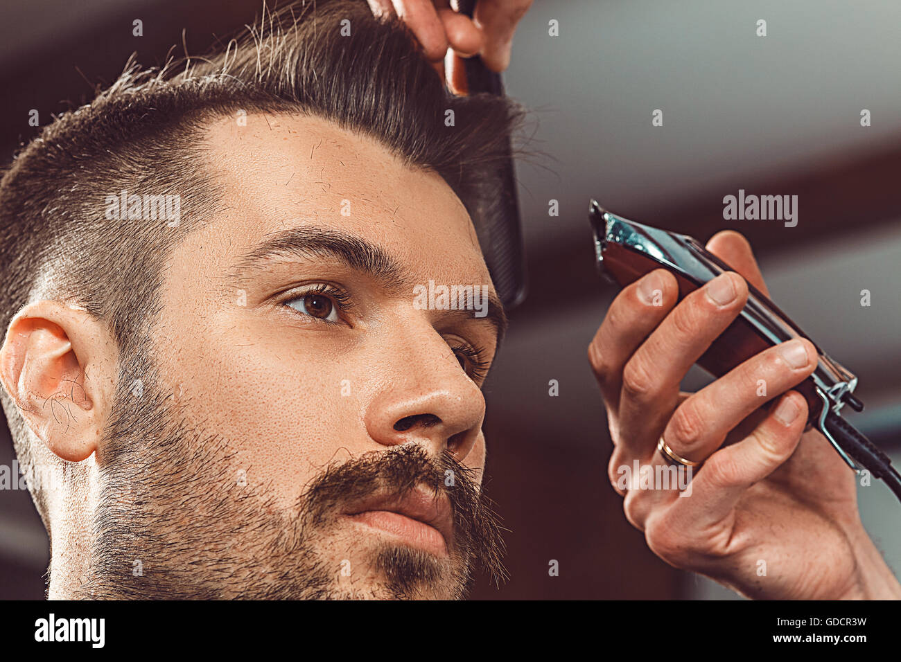 The hands of young barber making haircut to attractive man in ...
