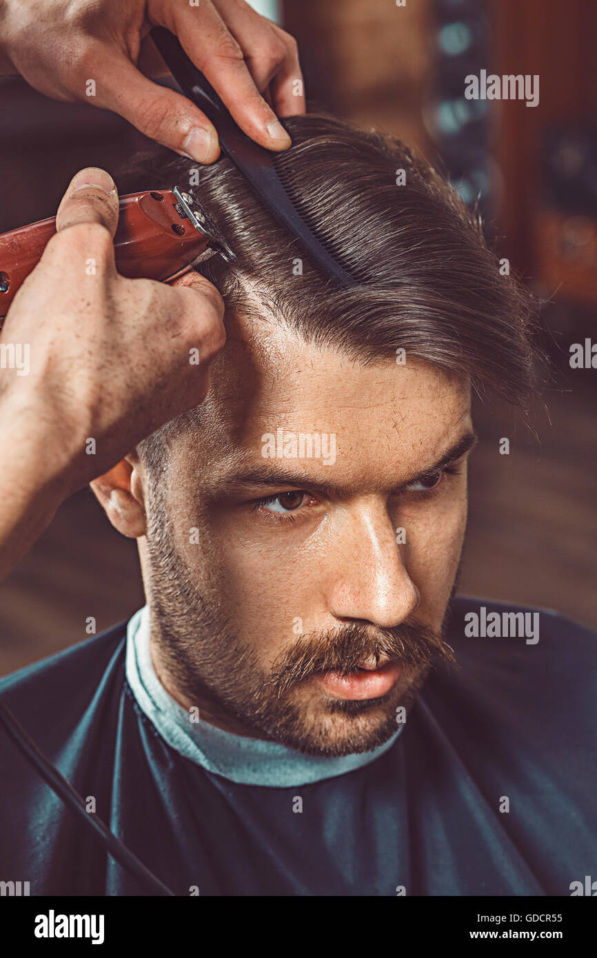 The hands of young barber making haircut to attractive man in ...