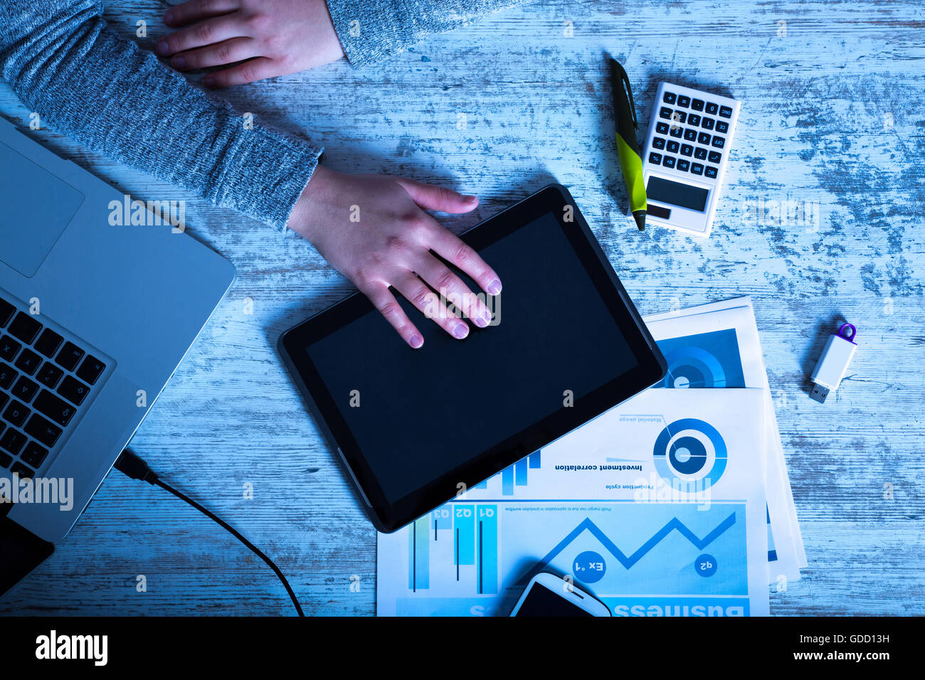 A working woman’s hand at night at a table with laptop, tablet and ...