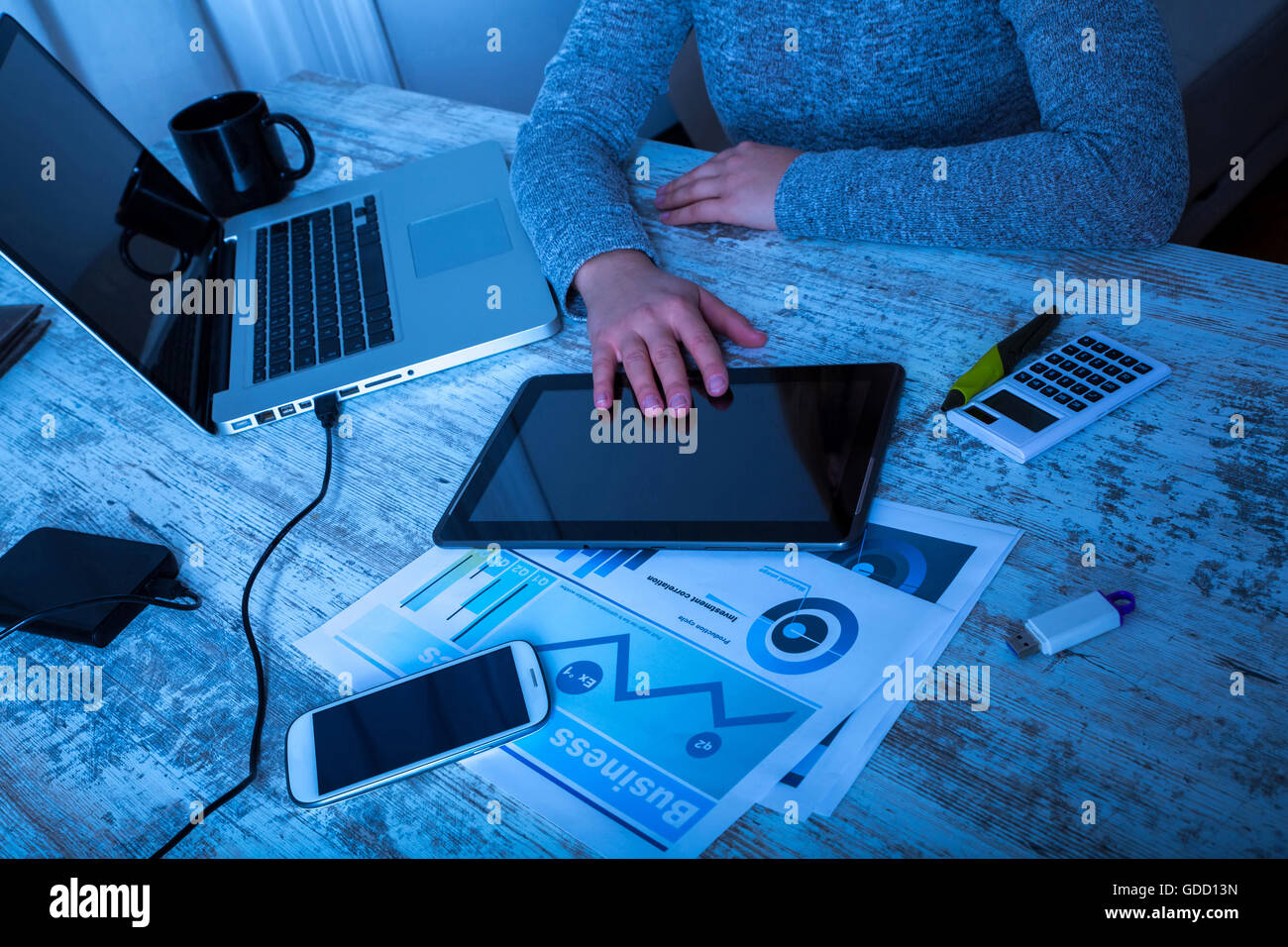 A working woman’s hand at night at a table with laptop, tablet and ...