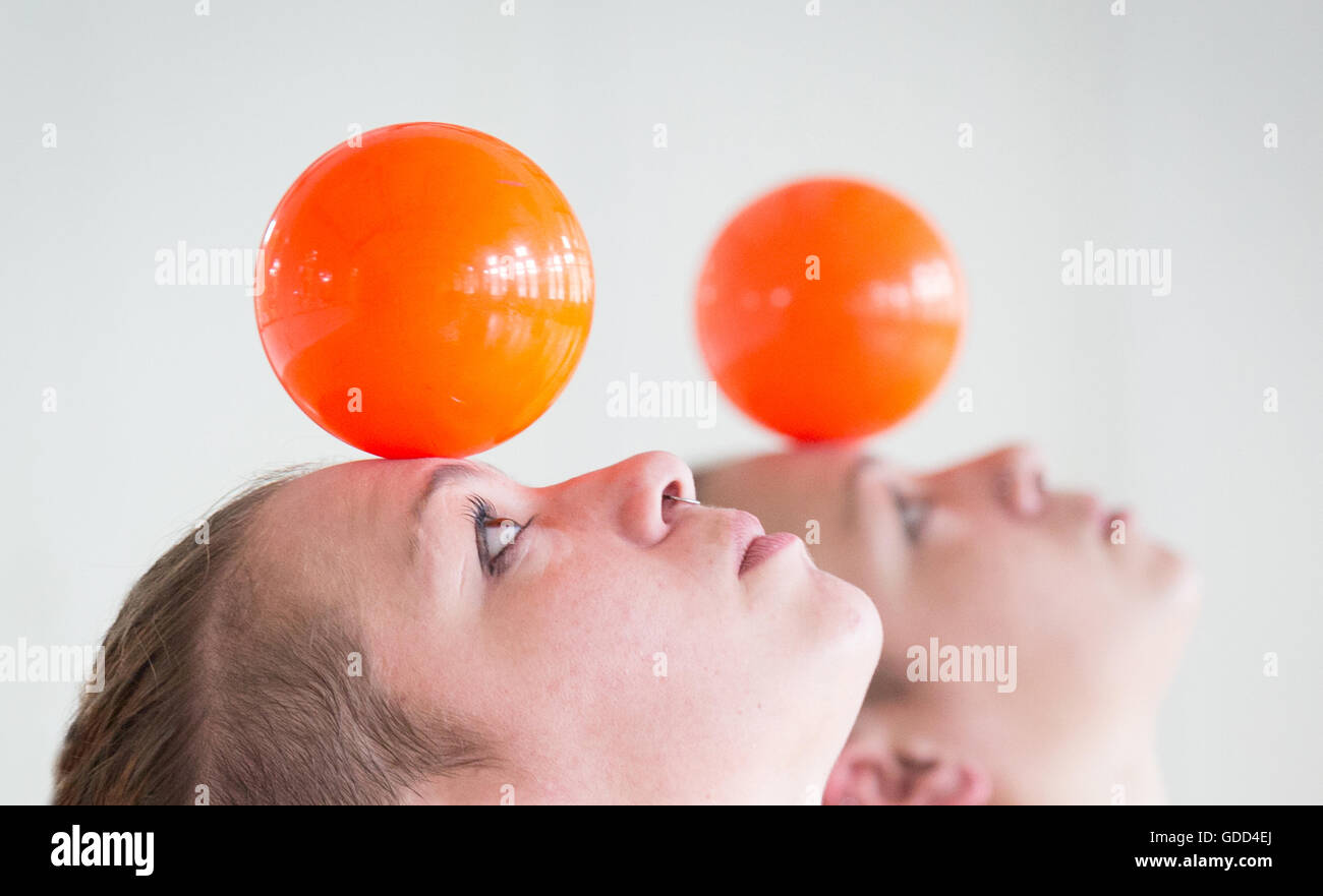Young female juggler balancing an orange ball on her head reflected in ...