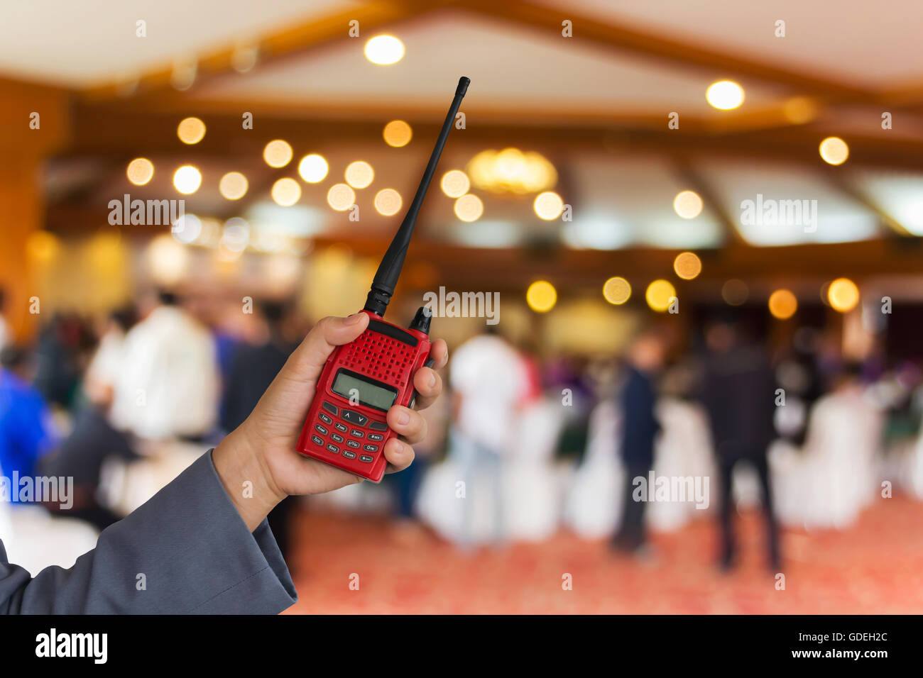 Red radio communication in hand with blurred people in convention hall ...