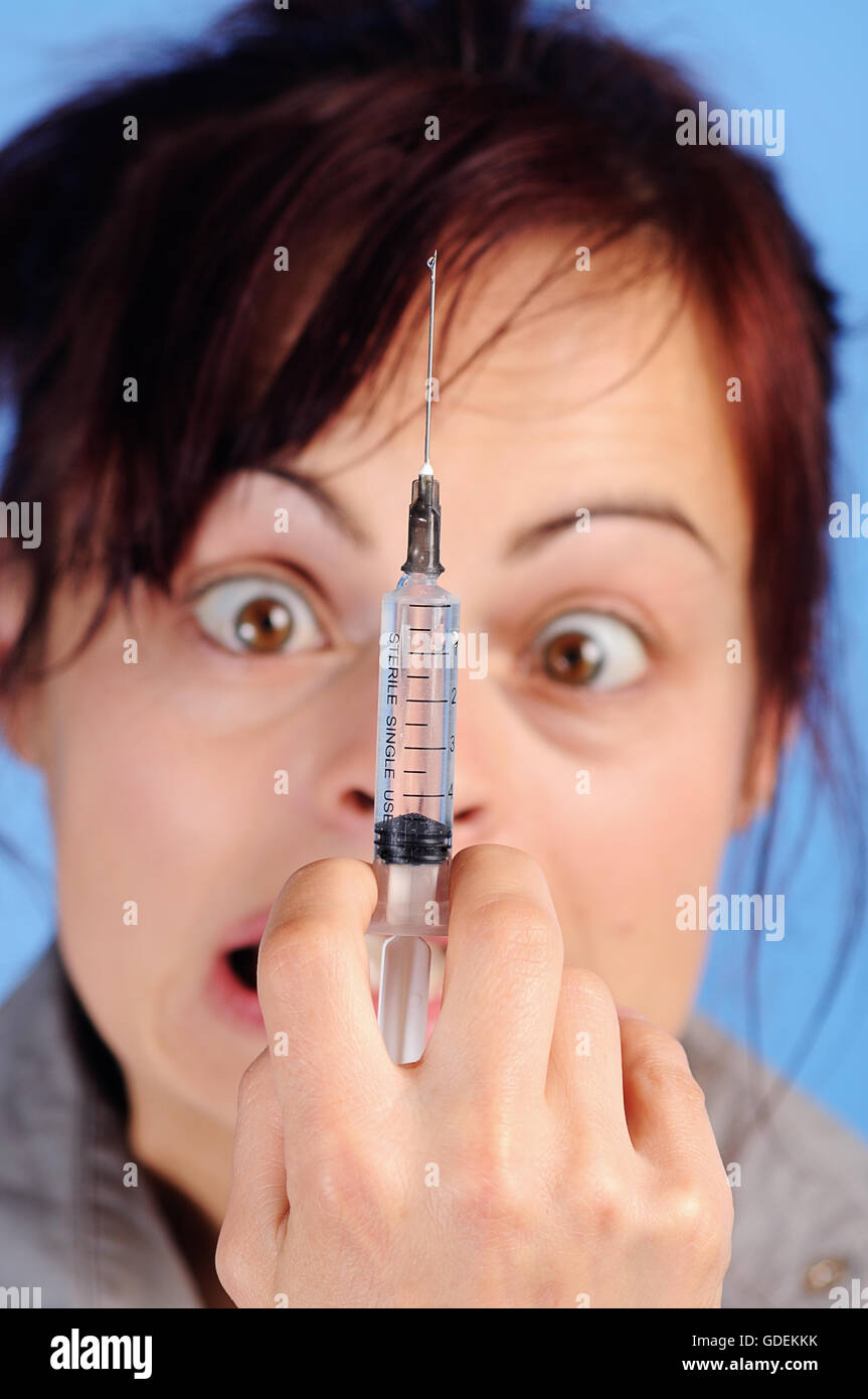 young woman holding a syringe and looking funny . Focus is on the ...