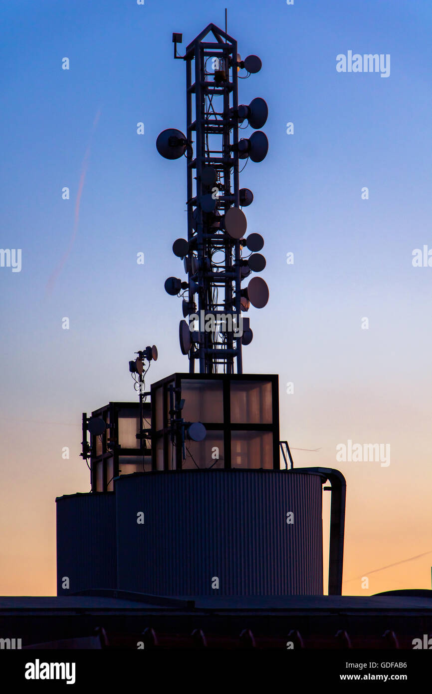 Telecommunication mast with microwave link on top roof at sunset ...